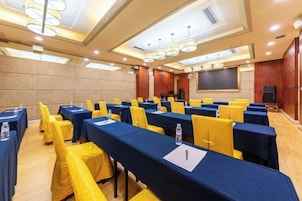 Uma sala de conferências com mesas, cadeiras, tela de projetor e área para apresentações.