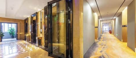Corredor de hotel com piso de mármore, portas de vidro e um longo hall.