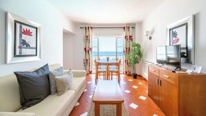Uma sala de estar moderna com sofá, mesa de centro, televisão e área de jantar com vista para o mar.