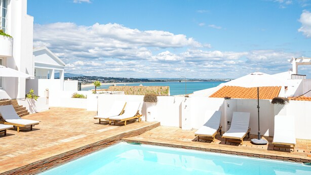 Uma área à beira da piscina com espreguiçadeiras, uma piscina e vista para o mar.