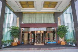 Entrada de hotel com porta giratória, grandes janelas e vasos de plantas.