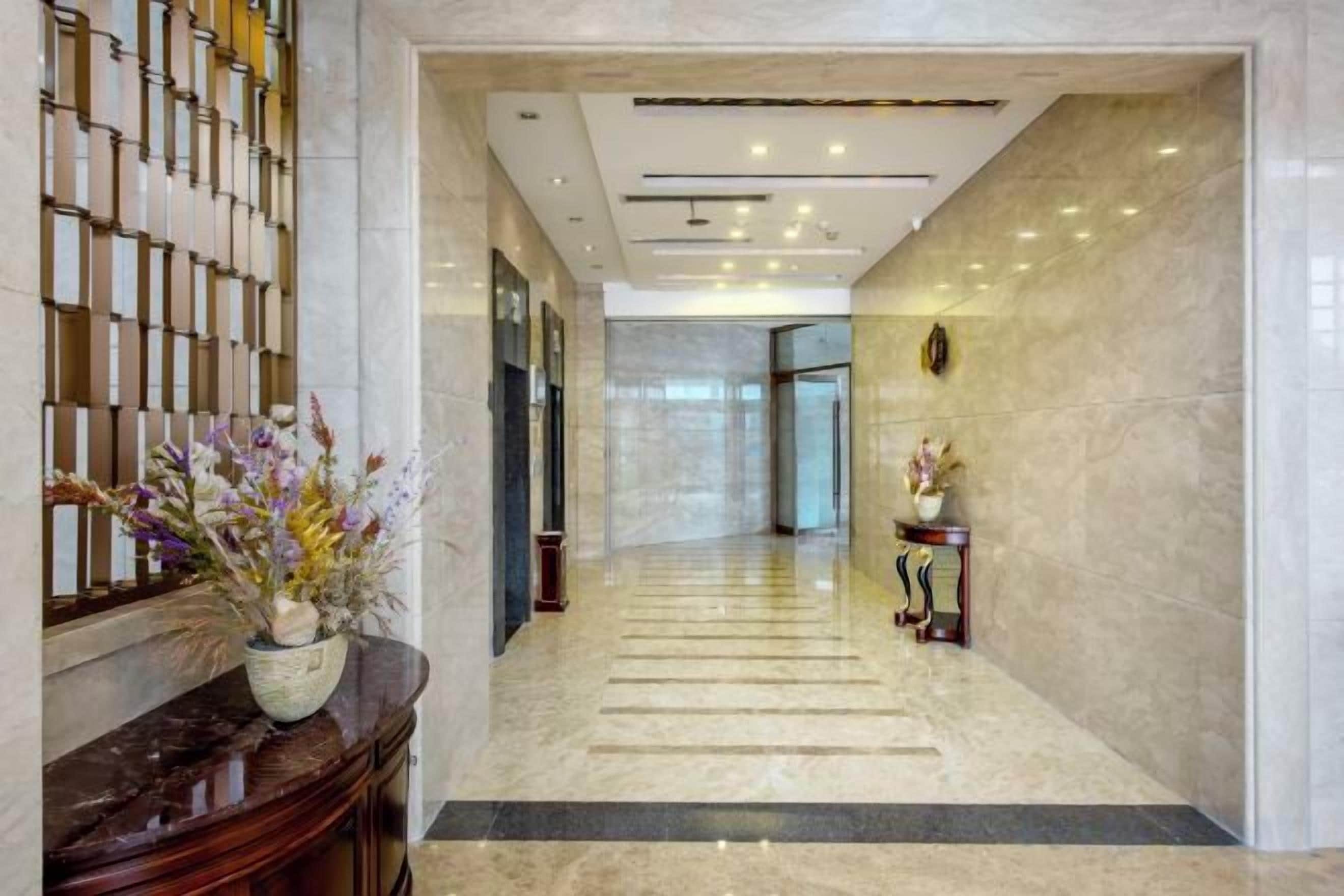 Um saguão de hotel com piso de mármore, balcão de recepção e um painel fixado na parede.