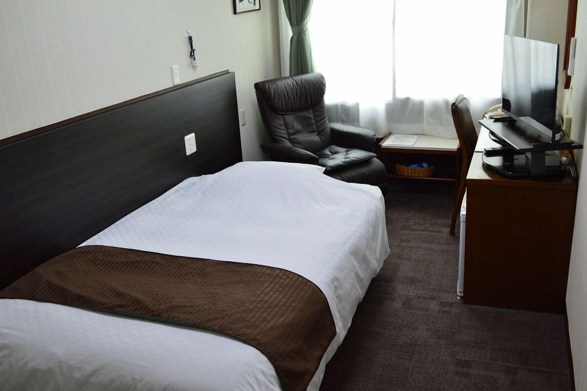 Quarto de hotel com cama, escrivaninha, cadeira e televisão.