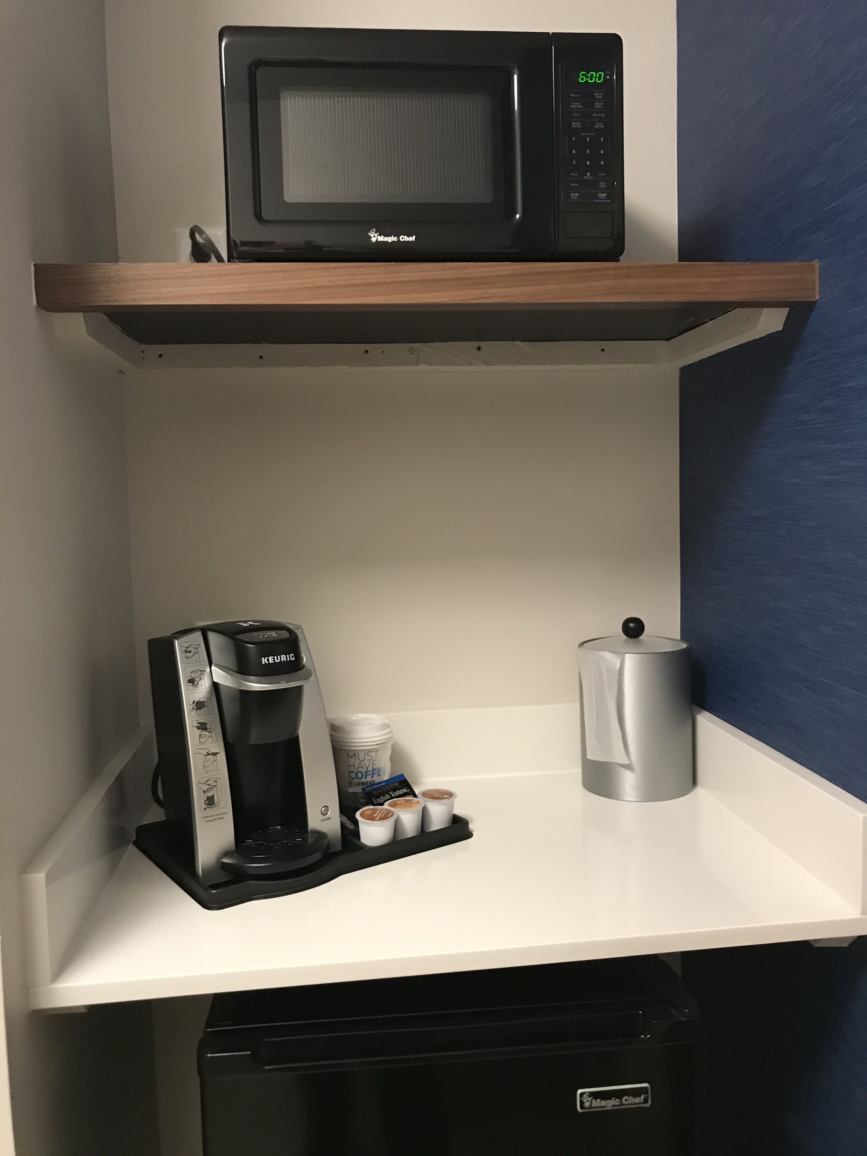 Uma cozinha compacta equipada com micro-ondas, cafeteira e lixeira.