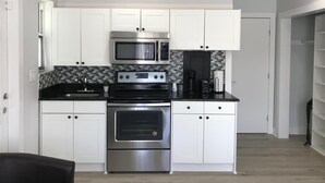 Uma cozinha moderna com armários brancos, forno de aço inoxidável, micro-ondas e máquina de café.