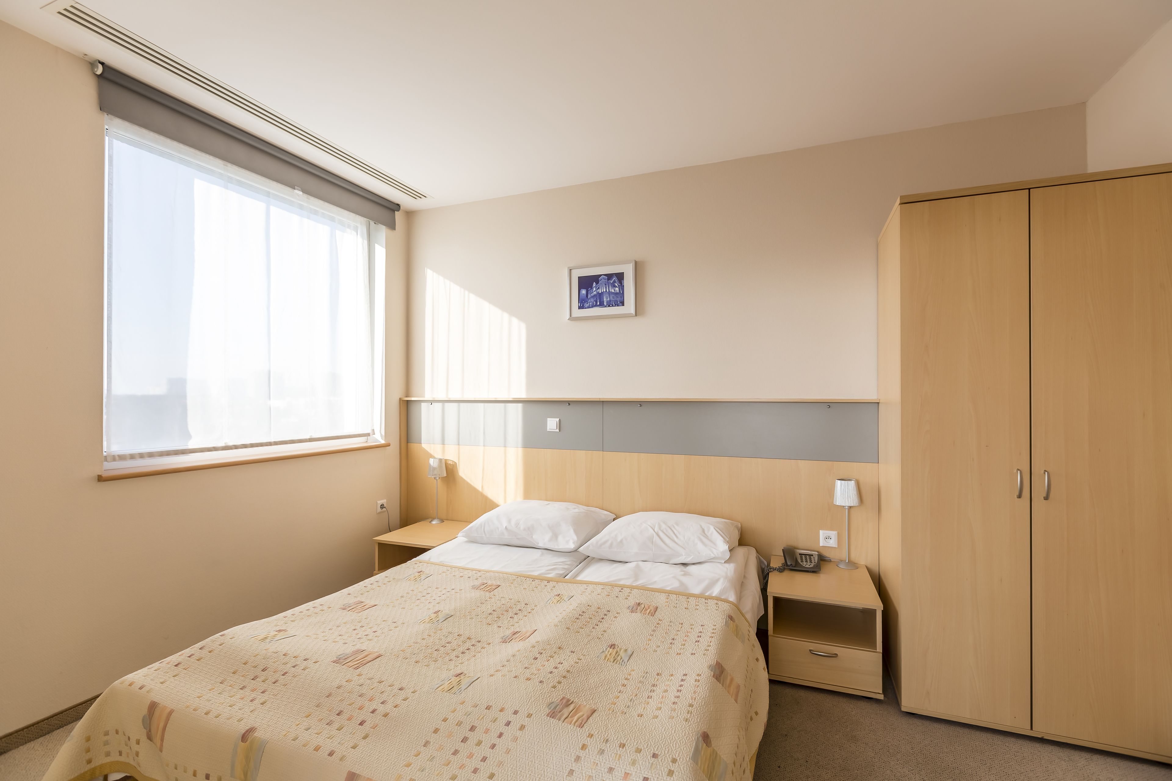 Quarto com cama, mesas de cabeceira, guarda-roupa e janela com persianas.