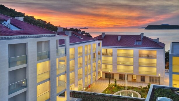 Um hotel moderno com vários andares, grandes janelas e vista para o mar ao pôr do sol.
