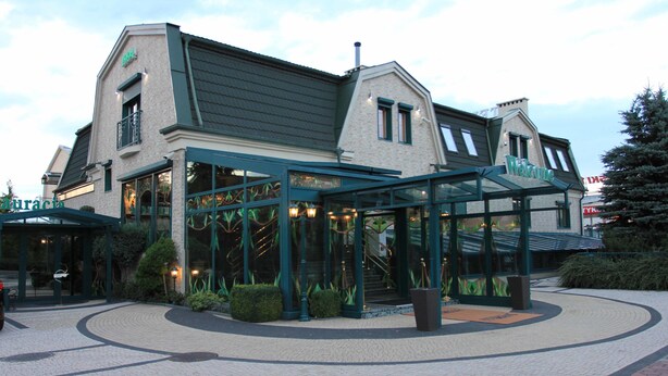 Um hotel com entrada de vidro, área de estar coberta ao ar livre e um caminho de tijolos.