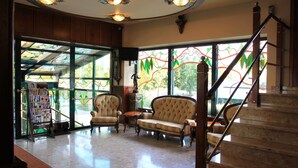 Um hall com escada, área de estar com poltronas, suporte para revistas e janelas amplas com vista para o verde.
