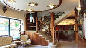 Uma escadaria imponente com corrimãos de madeira e um candelabro, que dá acesso a uma biblioteca com estantes.