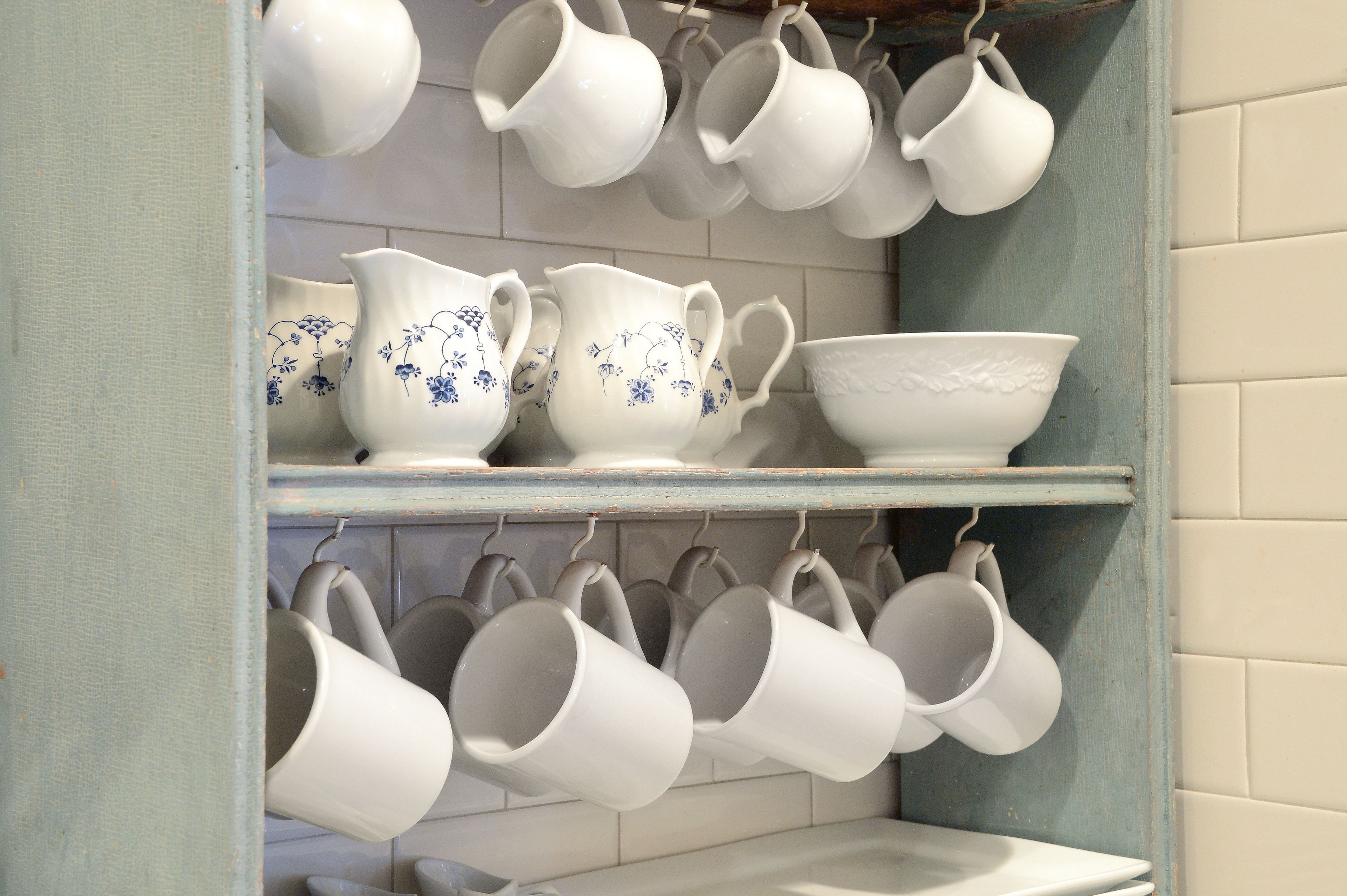 Uma prateleira na cozinha com canecas e jarras de cerâmica branca.