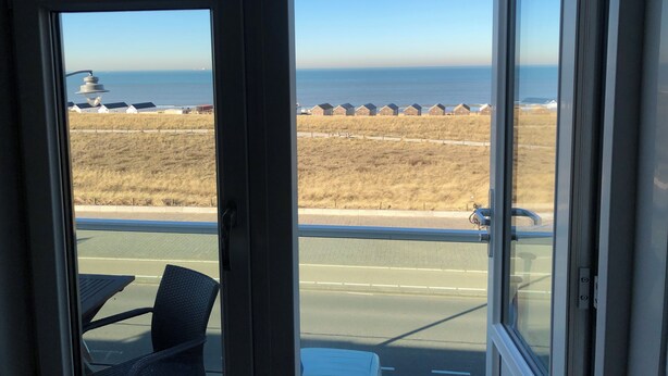 Vista de um quarto com uma grande janela para a praia, com cabanas e o oceano.