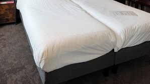 Quarto de hotel com uma cama grande, cabeceira, duas mesas de cabeceira com luminárias, uma cadeira e um quadro na parede com uma praia.