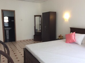 Quarto de hotel com cama, guarda-roupa, espelho, pia e cadeira.