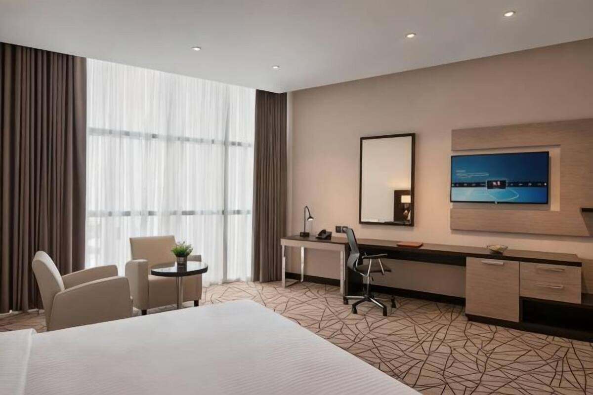 Quarto de hotel com uma cama grande, uma escrivaninha com cadeira, televisão e janela com cortinas.