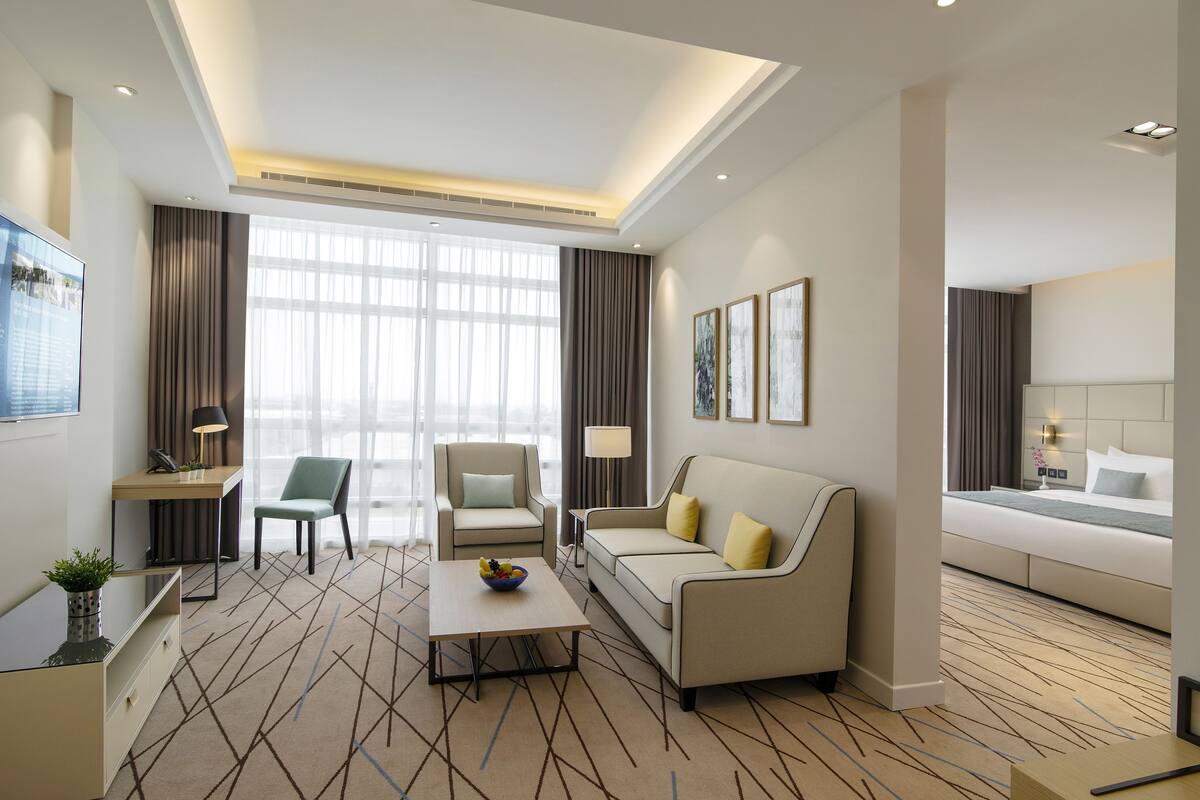 Quarto de hotel moderno com sofá, poltrona e escrivaninha com luminária.