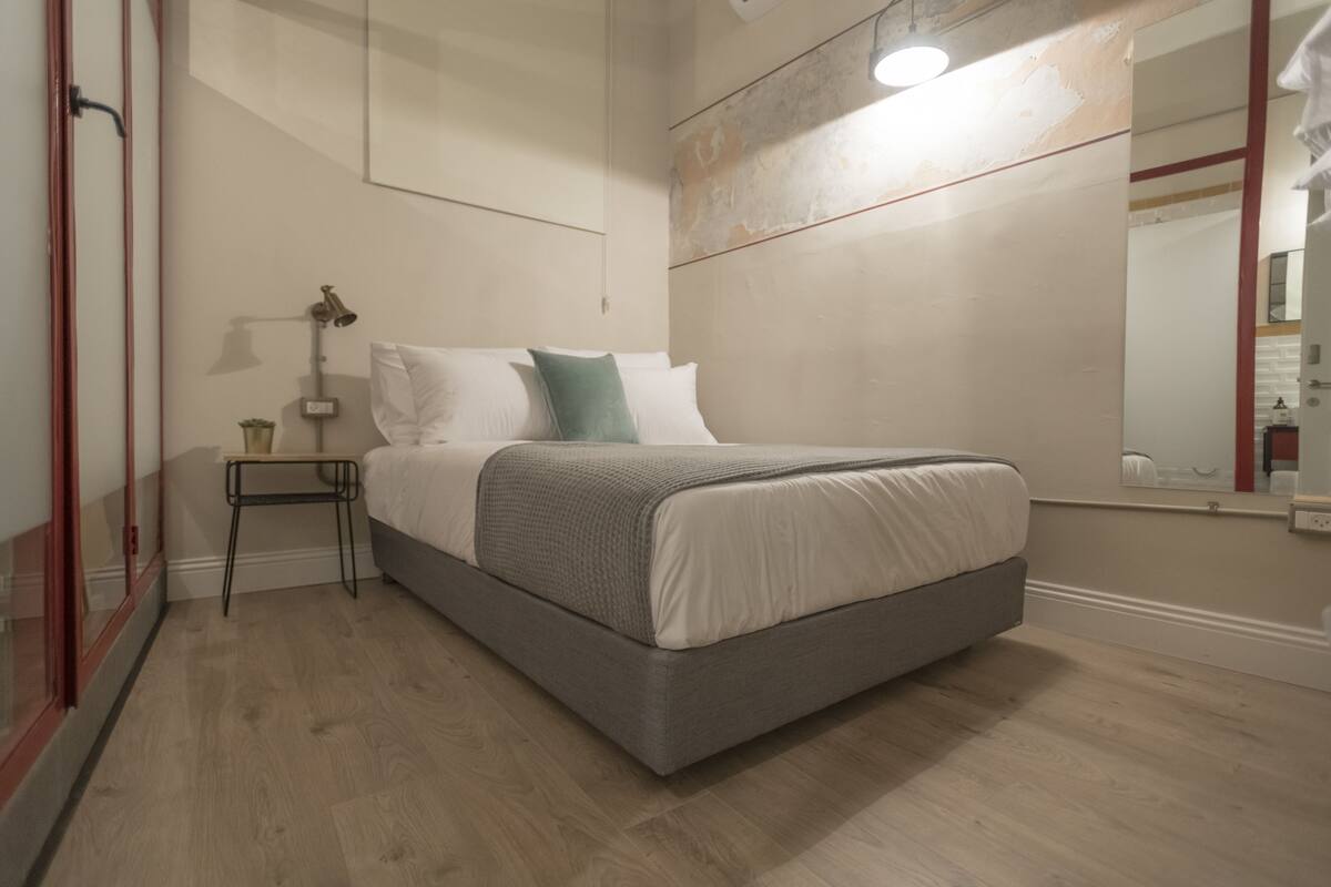 Quarto moderno com cama, mesa de cabeceira, abajur e um espelho grande.