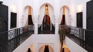 Interior com vários níveis, arcos ornamentados, uma escadaria central e uma planta de cacto.