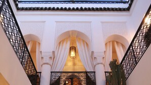 Um interior espaçoso com um arco central, uma escadaria com grades ornamentadas e uma grande planta em vaso.