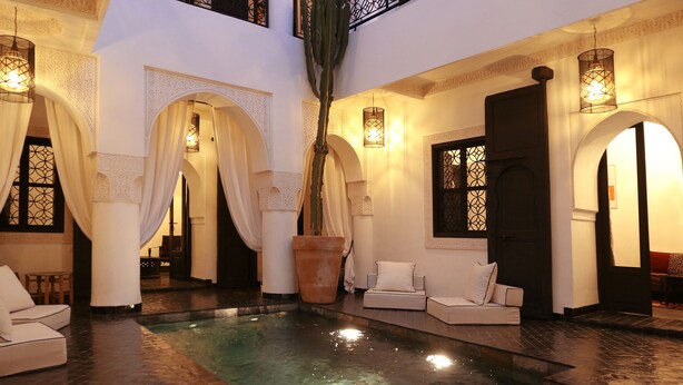 Uma área de piscina interior luxuosa, com piscina translúcida, sofás brancos e detalhes arquitetónicos elaborados.