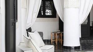 Uma área de estar moderna com um sofá branco, um candeeiro pendente e uma janela decorativa com cortinas brancas.