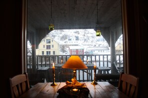 Uma mesa de madeira com uma lâmpada e velas, com vista para uma paisagem nevada e edifícios.