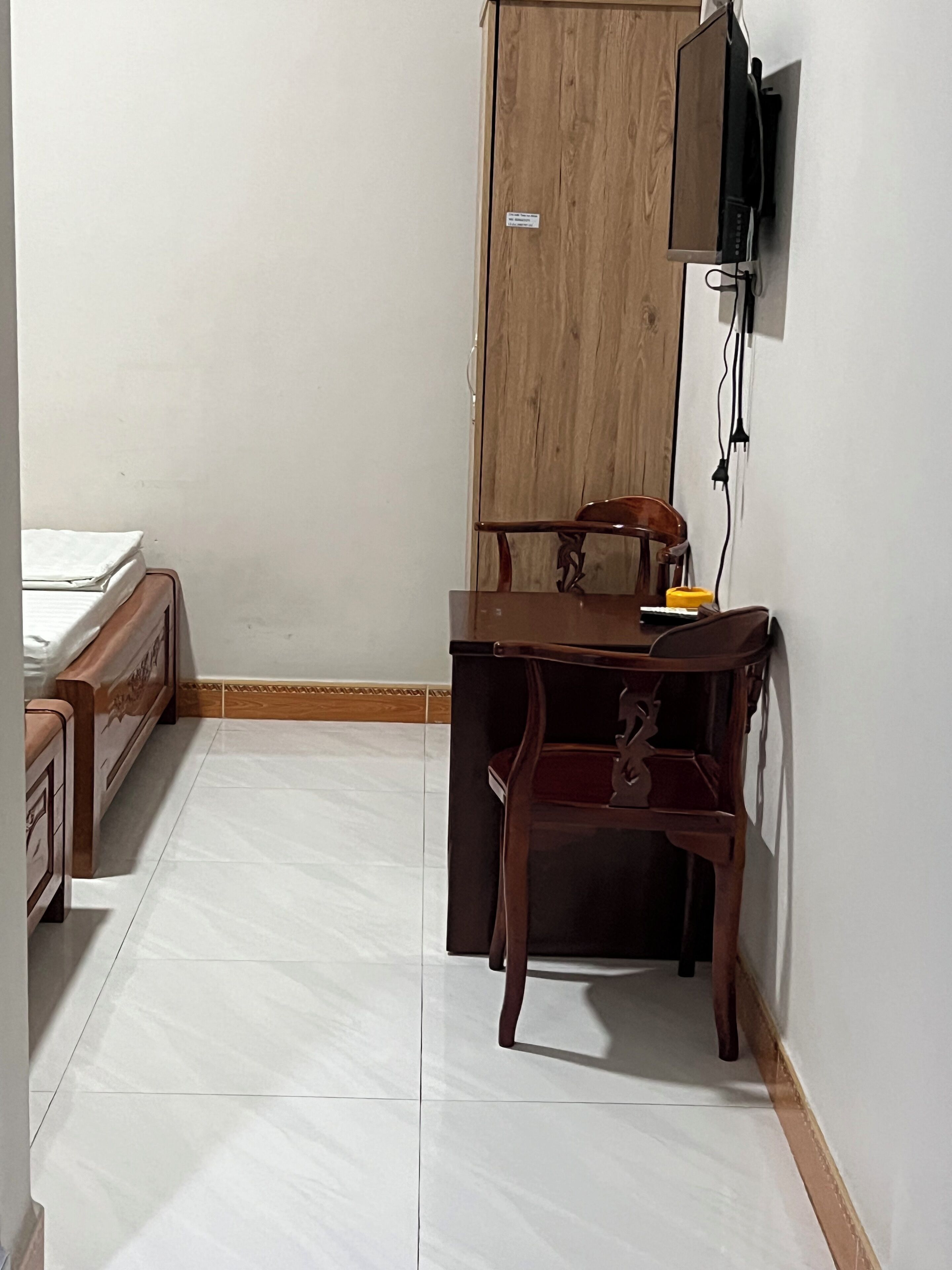 Um quarto pequeno com uma escrivaninha de madeira, uma cadeira, uma cama e uma TV fixada na parede.
