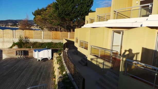 Um edifício moderno com um deck de madeira, área de estar externa e vista para o mar.