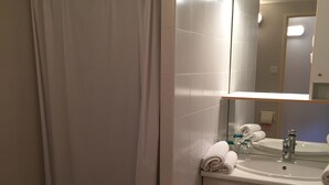 Casa de banho com cortina de chuveiro, pia, espelho e porta-toalhas.