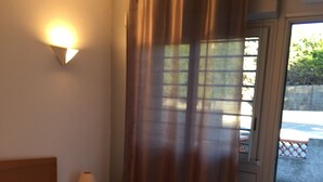Quarto com cama, mesa de cabeceira, abajur, janela com cortinas e aparelho de ar condicionado.