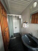 Casa de banho com porta de madeira, chuveiro com porta de vidro, lavatório preto e espelho sobre o lavatório.