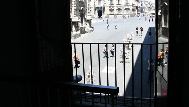Vista de varanda com vista para uma praça pública, prédios e pessoas.