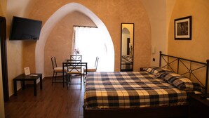 Quarto com cama, escrivaninha, cadeiras, televisão e espelho.