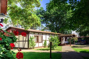 Um edifício tradicional com telhado de telhas, varanda de madeira e um pequeno jardim com flores vermelhas.