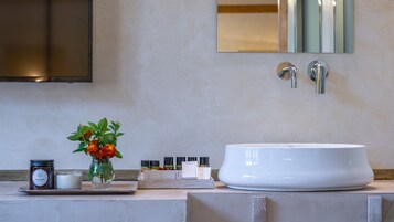 Casa de banho com uma grande pia branca, um espelho e um pequeno vaso de flores no balcão.