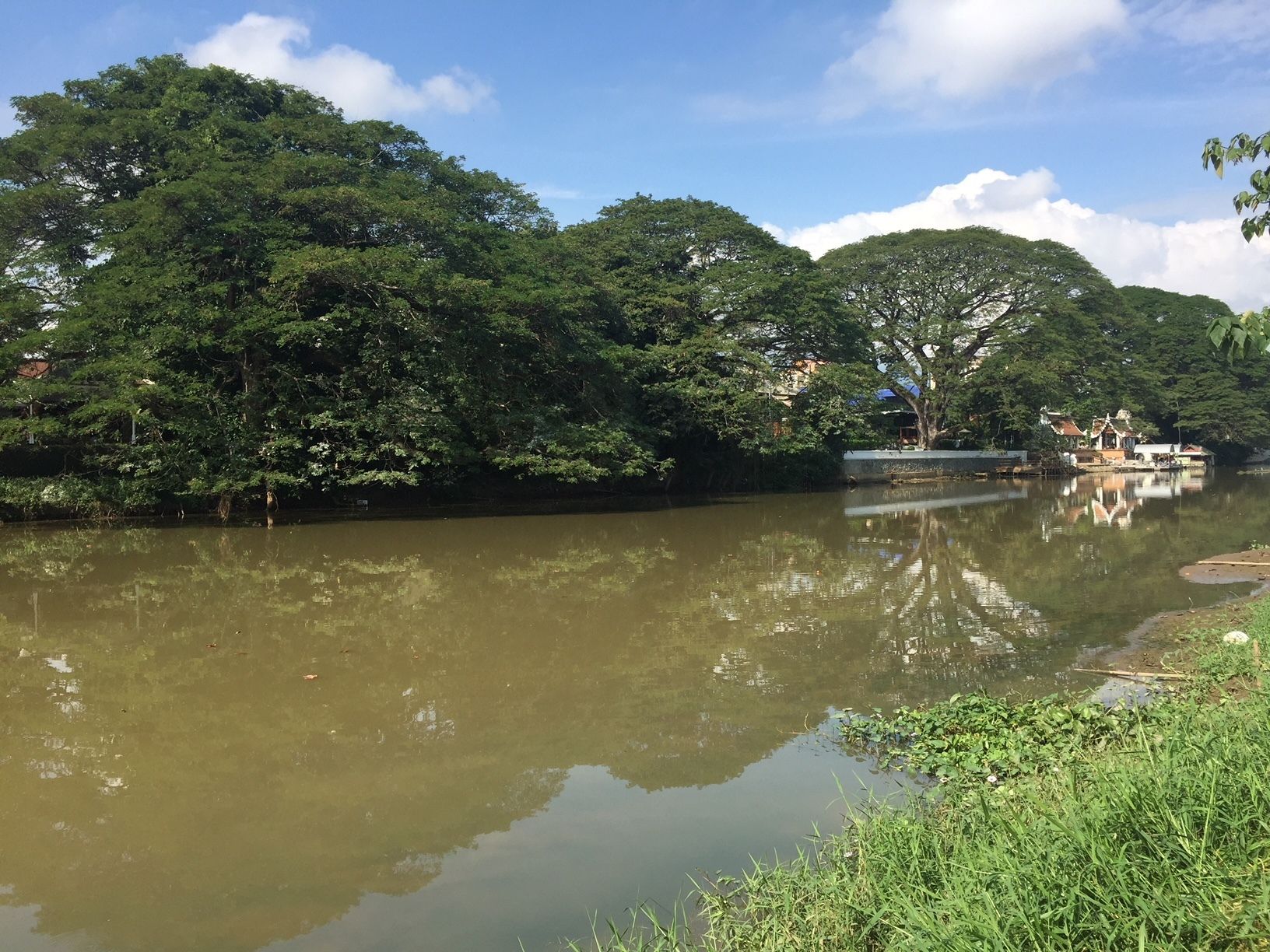 Um rio calmo com vegetação densa e um pequeno edifício de arquitetura tradicional na margem direita.
