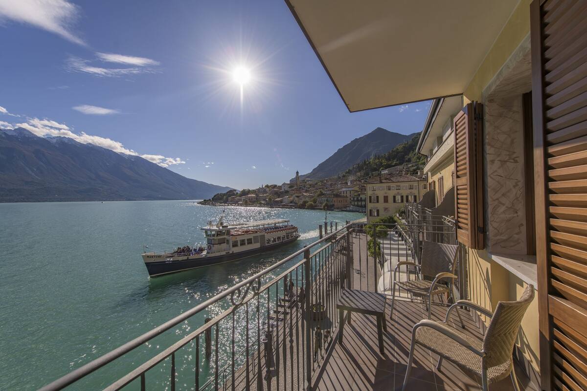 Uma varanda com vista para um lago, um barco e montanhas ao fundo.