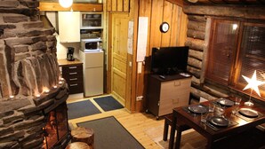Interior acolhedor de uma cabana com lareira de pedra, paredes de madeira, cozinha e mesa de jantar posta para quatro pessoas.