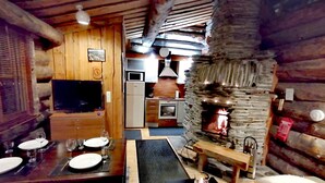 Interior rústico de uma cabana com área de jantar de madeira, lareira de pedra, televisão e uma kitchenette.