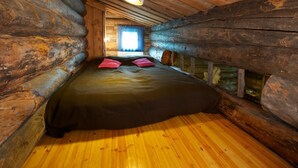 Quarto de cabana de tronco com cama, almofadas e janela com cortinas.