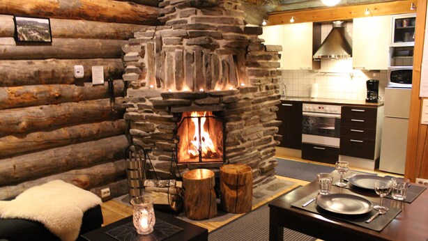Interior acolhedor de uma cabana de toras, com lareira de pedra, móveis de madeira e cozinha moderna.