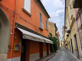 Uma rua estreita com edifícios de ambos os lados, incluindo uma loja com a placa que diz "TRATTORIA O'MASTO 1970".