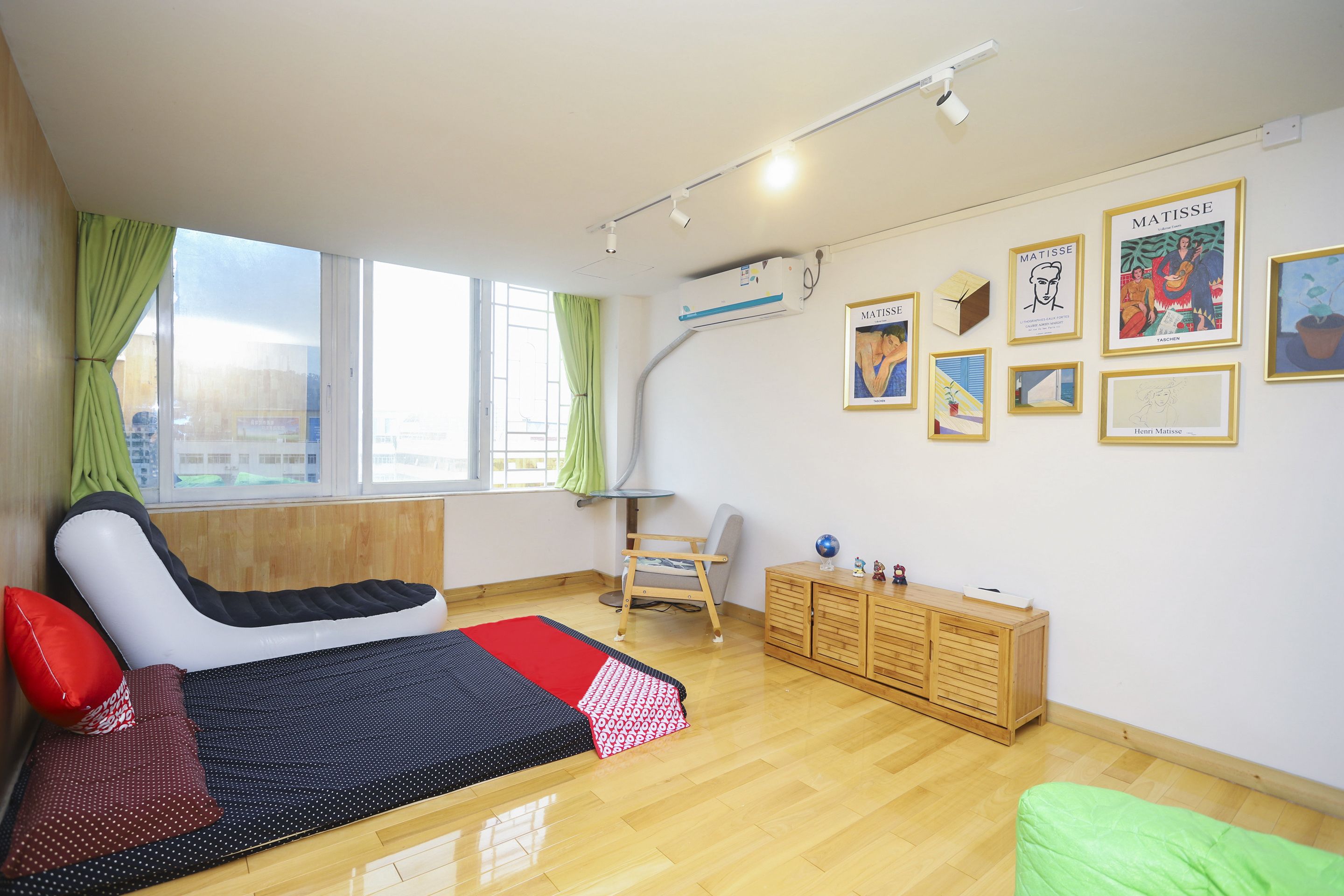 Quarto com uma cama, uma escrivaninha, uma cadeira e uma parede com obras de arte emolduradas.