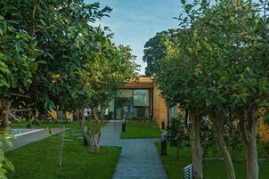 Um edifício moderno com fachada de vidro, cercado por um jardim bem cuidado e um caminho que leva à entrada.
