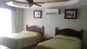 Quarto de hotel com duas camas de solteiro, ventoinha no teto, ar condicionado e quadros nas paredes.