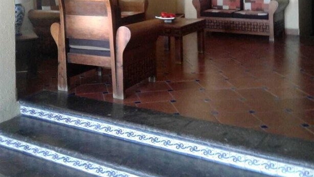 Uma sala ampla com uma mesa de jantar de madeira e cadeiras, um sofá estampado e piso de azulejos.