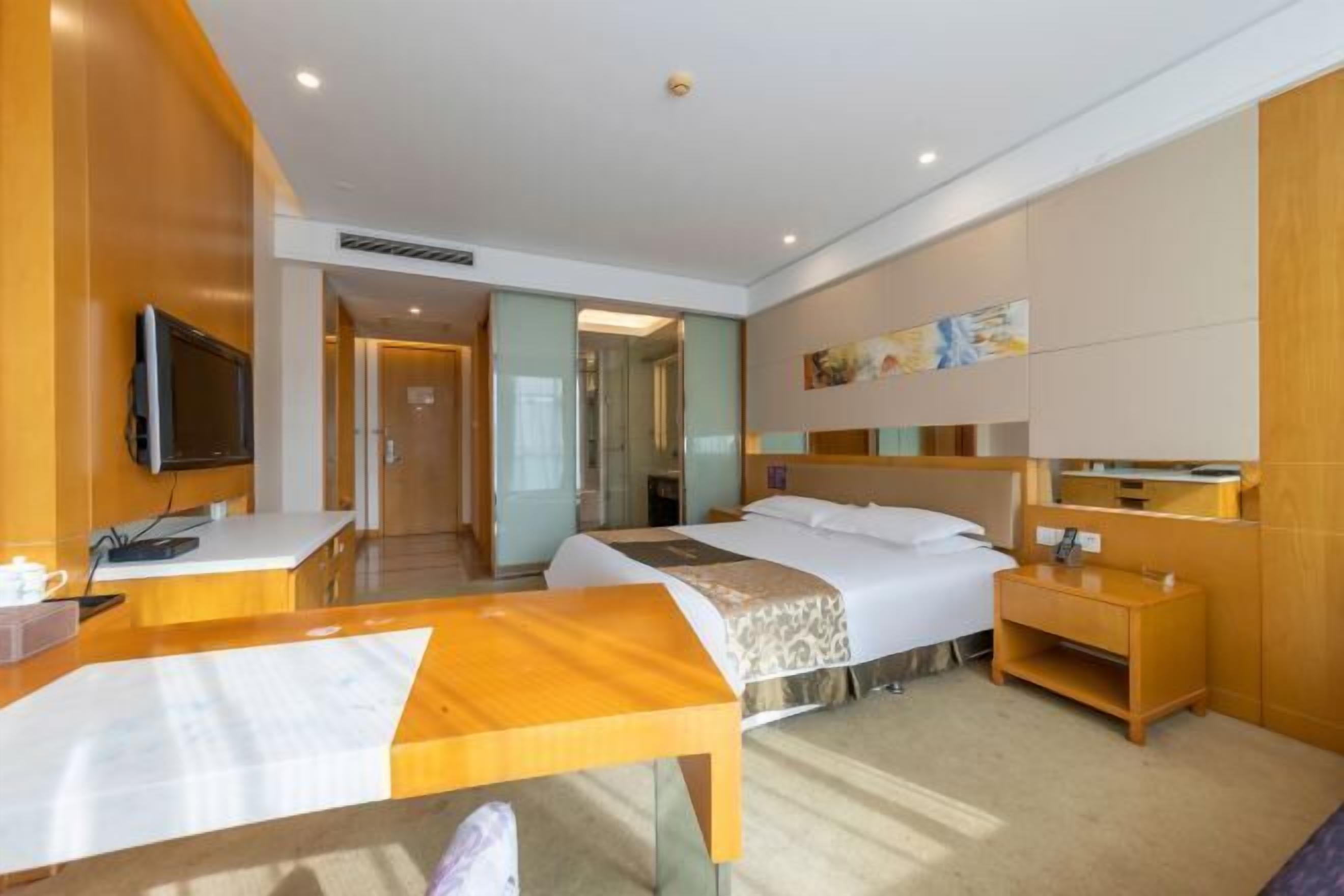 Quarto de hotel com cama, mesa de cabeceira, televisão e escrivaninha com cadeira.