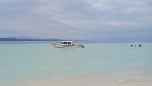 Um barco chamado 'ESMERALDA' ancorado perto de uma praia com águas turquesa cristalinas e montanhas ao longe.