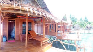 Uma cabana de madeira com telhado de palha, um deck de madeira e vista para o oceano.
