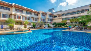 Uma piscina cercada por um edifício com vários andares, varandas, área de estar ao ar livre e vegetação.